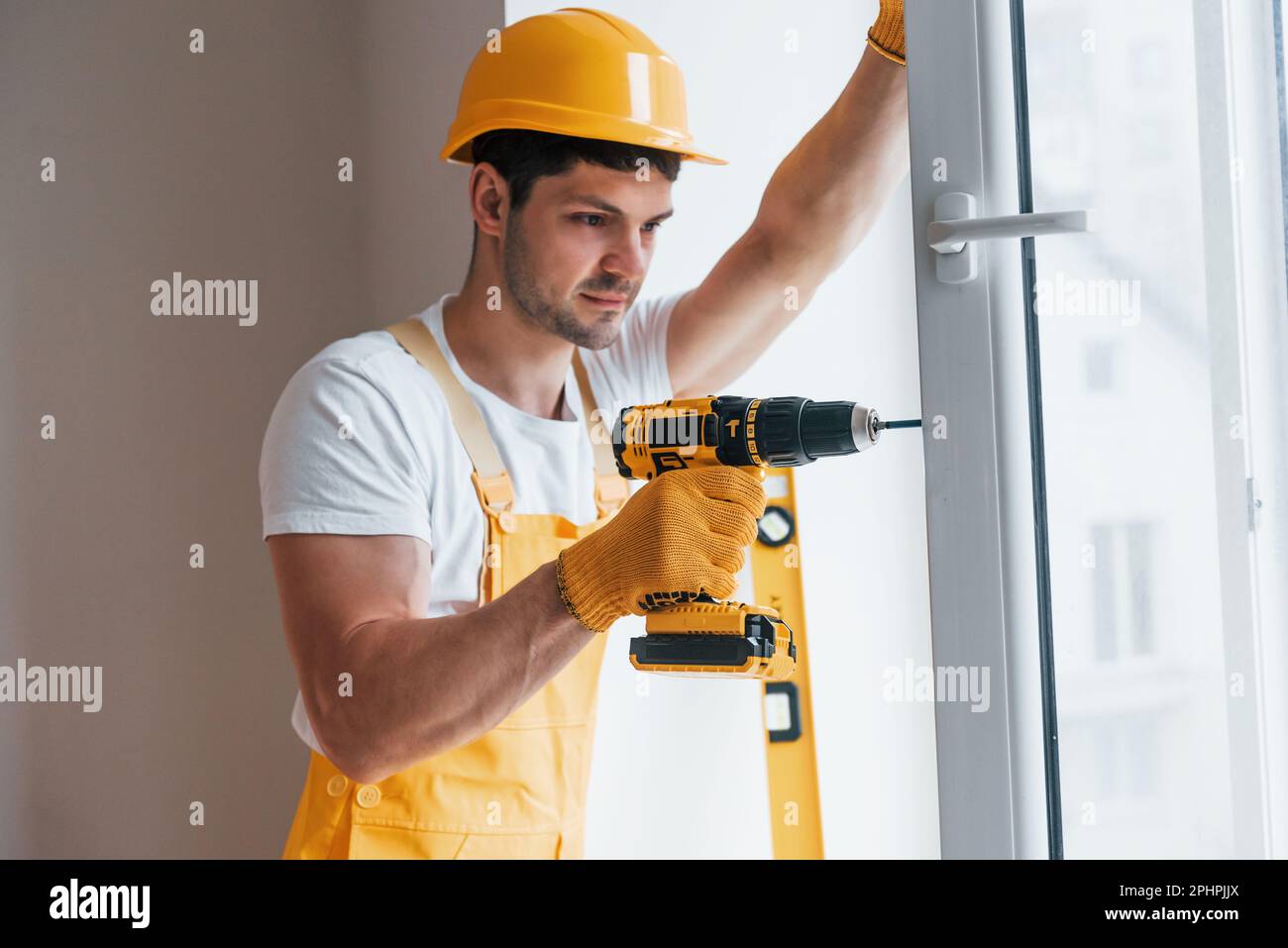 Handyman in yellow uniform installs new window by using automatic ...