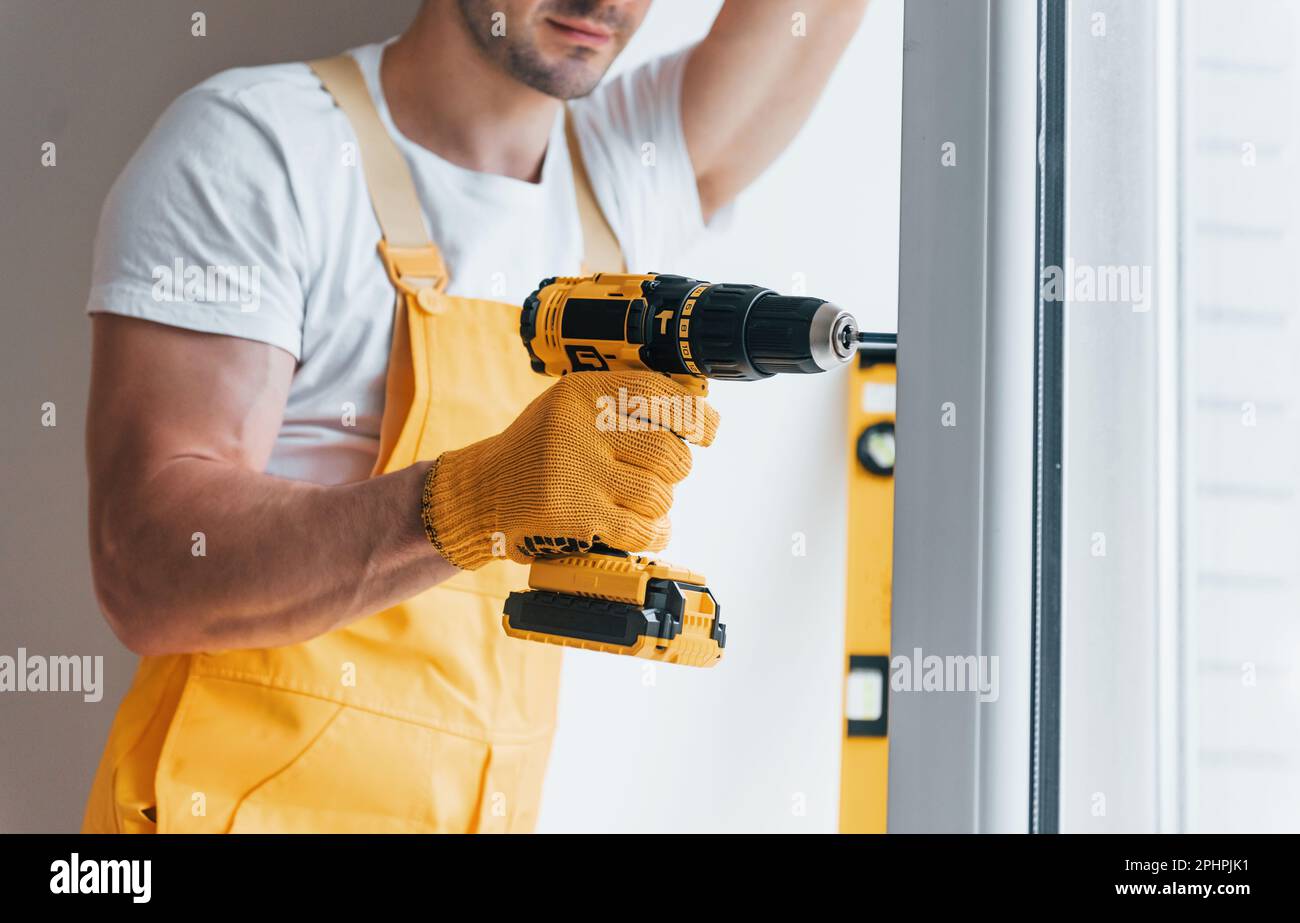 Handyman in yellow uniform installs new window by using automatic ...