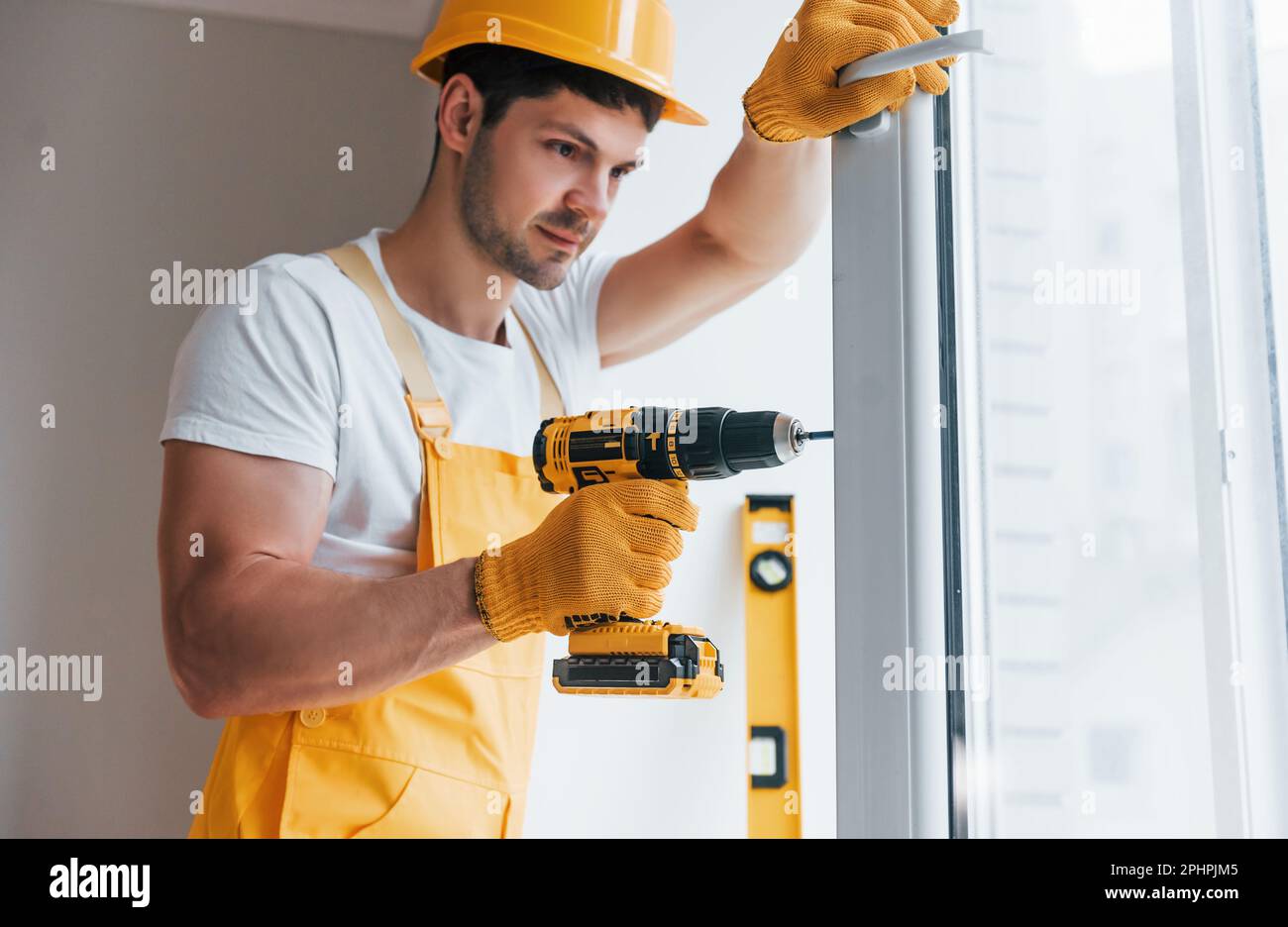 Handyman in yellow uniform installs new window by using automatic ...