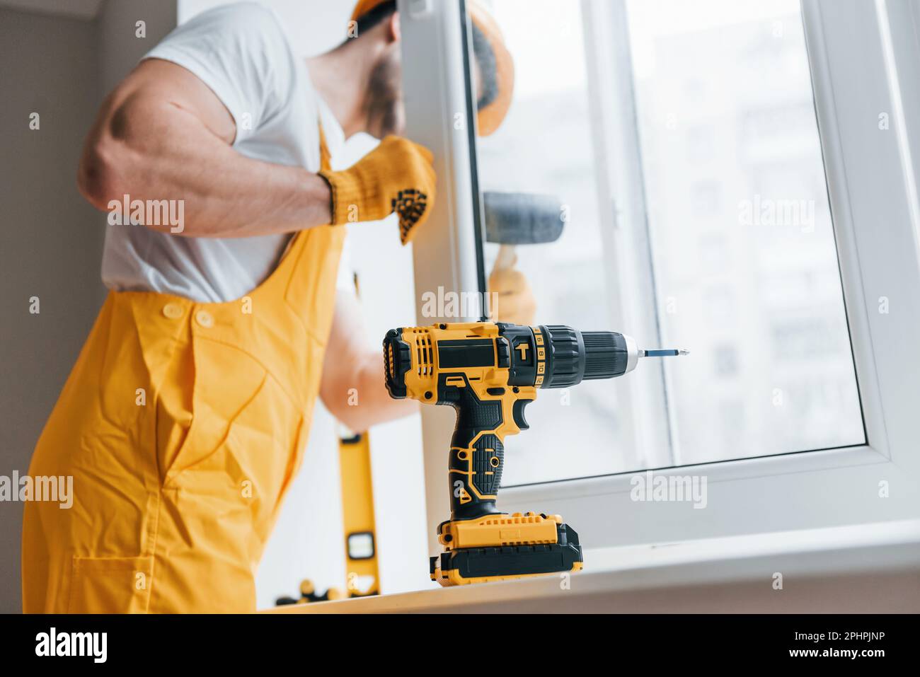 Handyman in yellow uniform installs new window by using automatic ...
