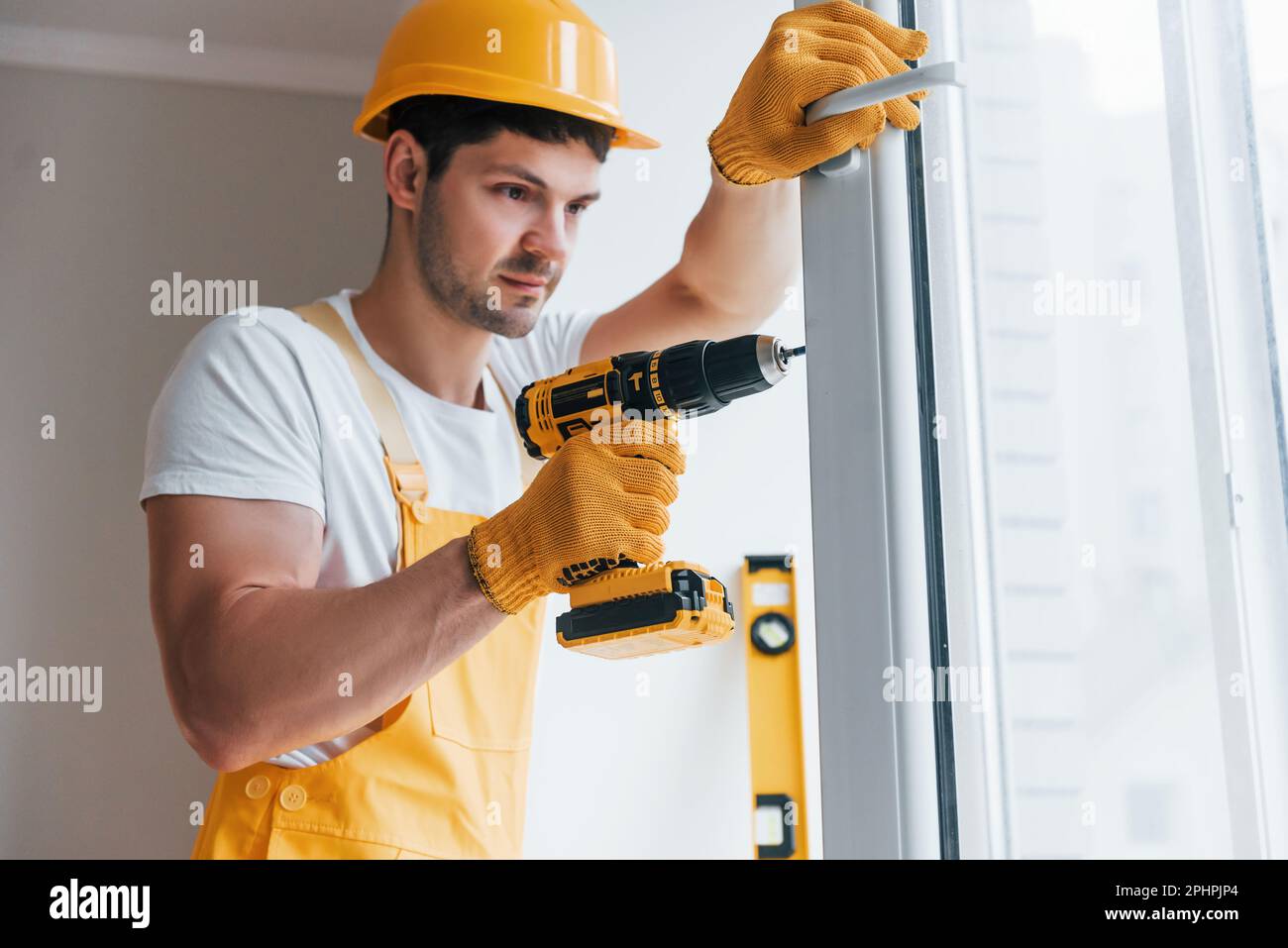 Handyman in yellow uniform installs new window by using automatic ...