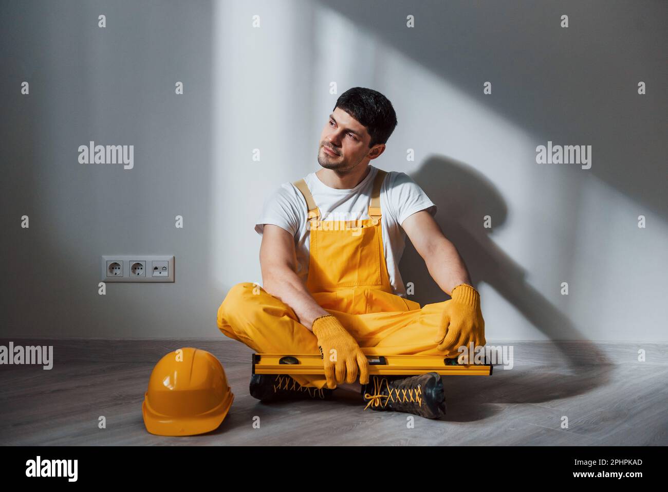 Tired handyman in yellow uniform sits indoors and takes break. House ...