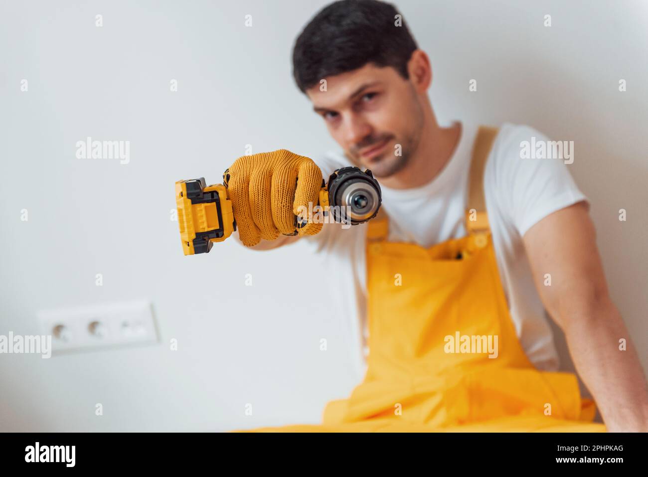Handyman in yellow uniform standing against white wall with automatic ...