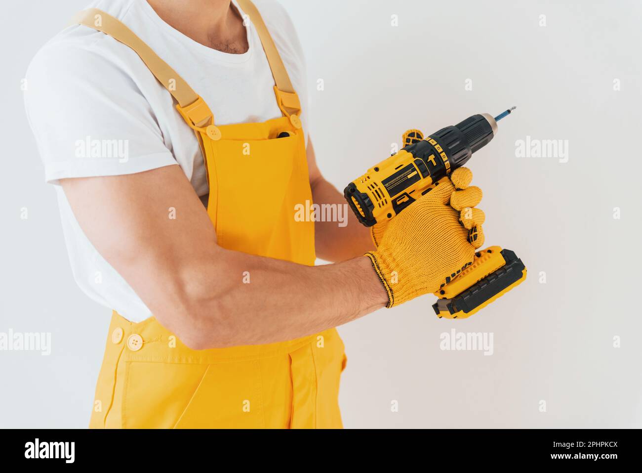 Handyman in yellow uniform standing against white wall with automatic ...