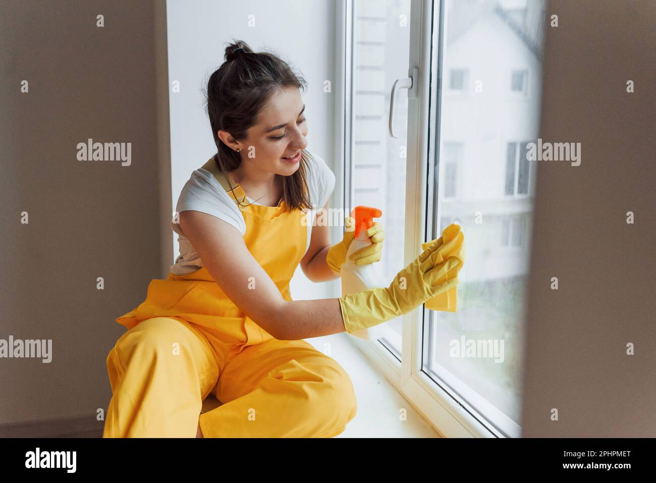 Housewife in yellow uniform cleaning windows. House renovation ...