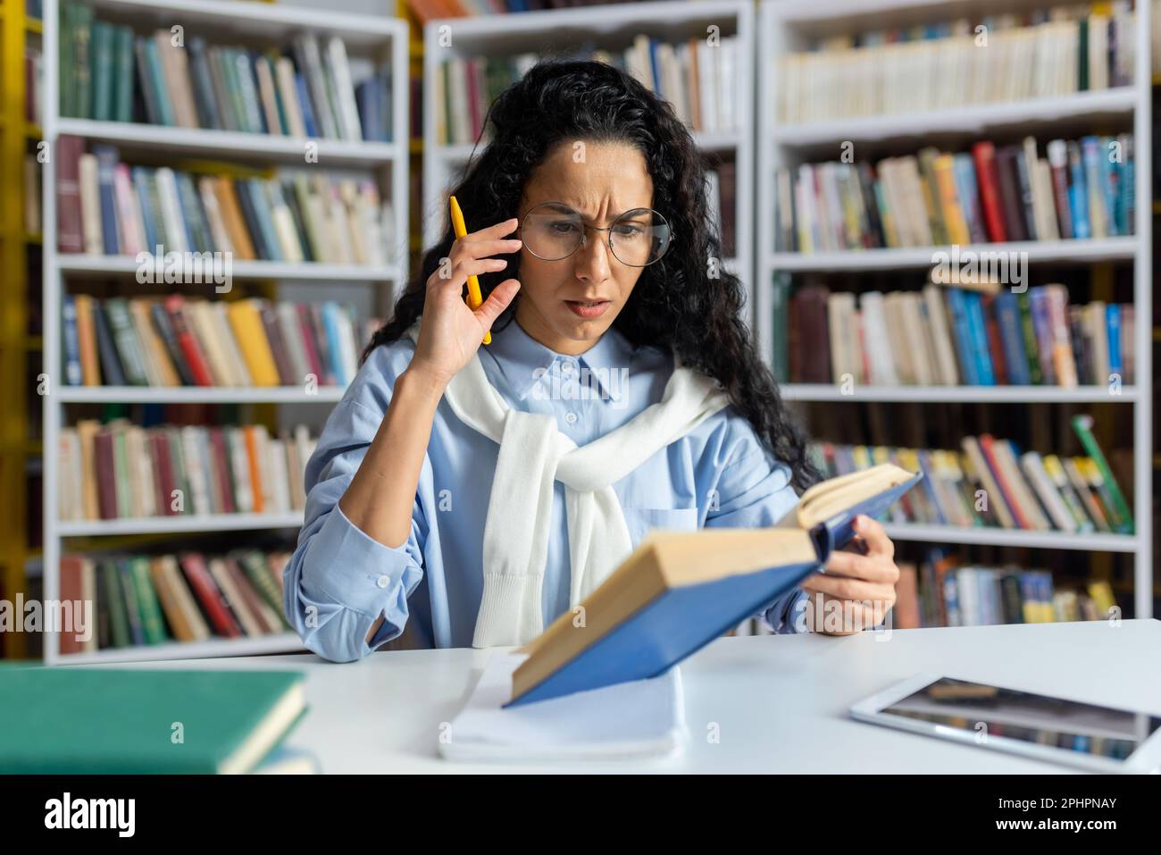 Tired overworked female student studying alone in university library ...