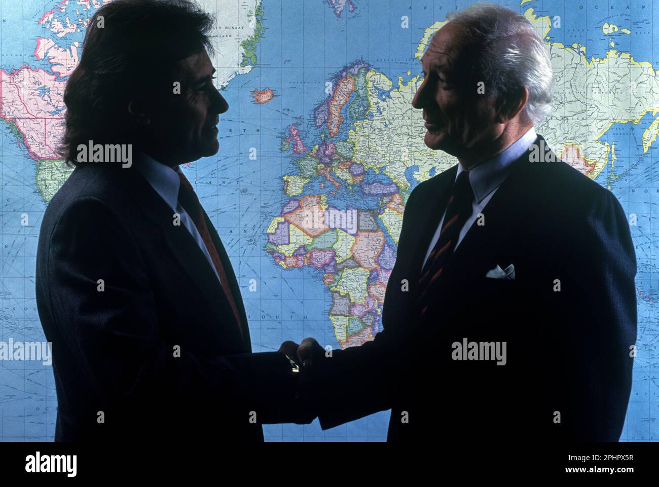 1990 HISTORICAL SILHOUETTED MALE OFFICE WORKERS HANDSHAKE AT WORLD MAP ...