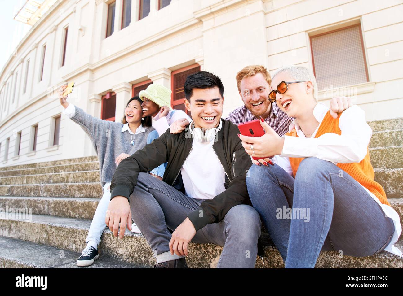 Smiling woman showing something on mobile phone to multi-ethnic friends ...