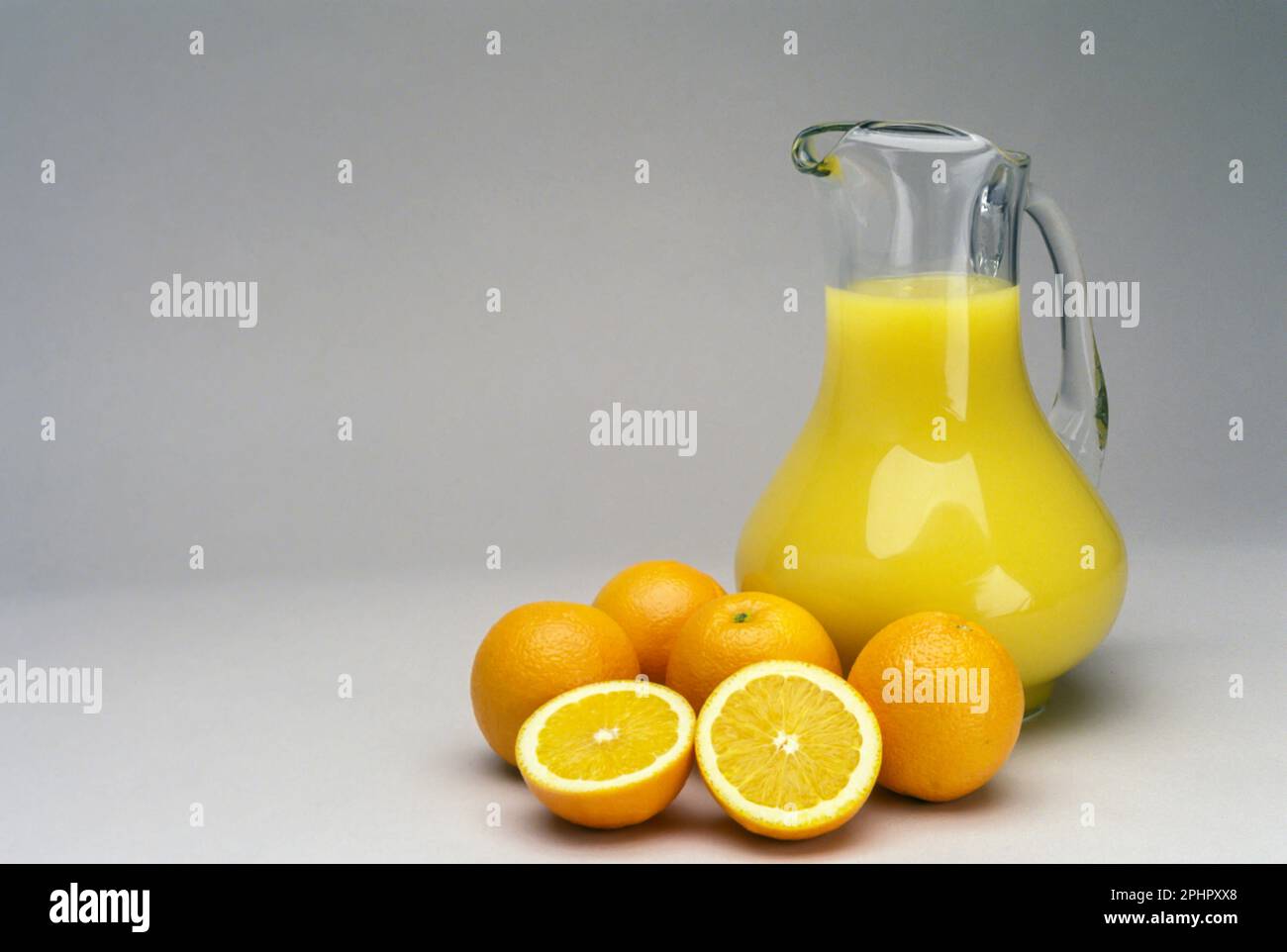GLASS PITCHER OF ORANGE JUICE WITH FRESH CUT ORANGES ON PLAIN WHITE ...