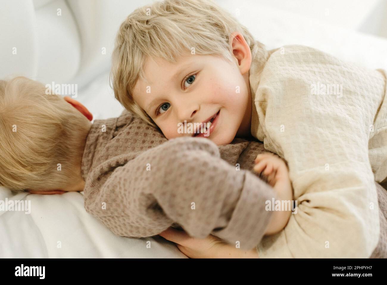 The brothers lie in dressing gowns in a white bed, play, hug, smile ...