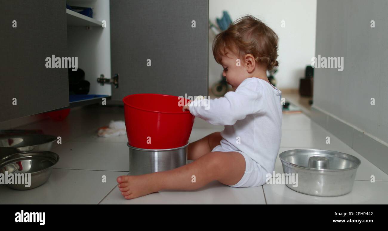 Cute baby on kitchen floor playing with kitchen utensils, playful one ...