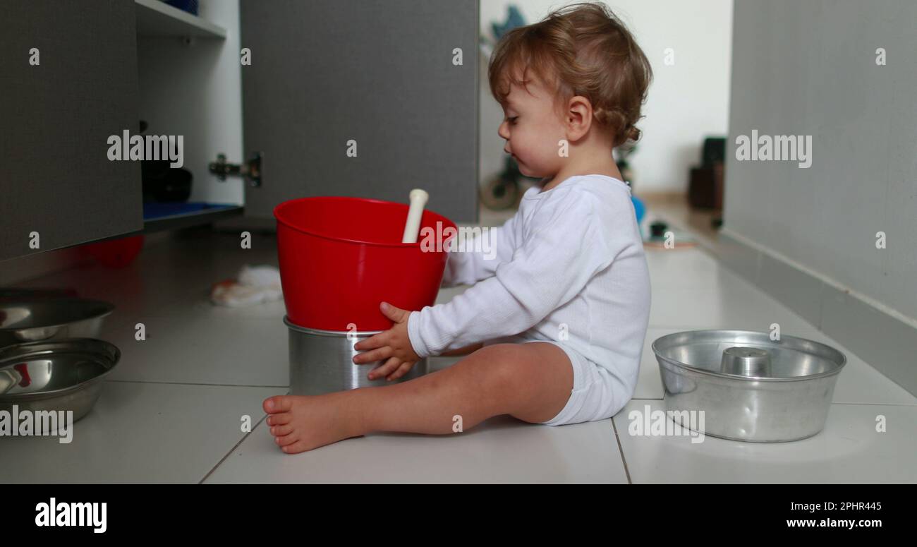 Cute baby on kitchen floor playing with kitchen utensils, playful one ...