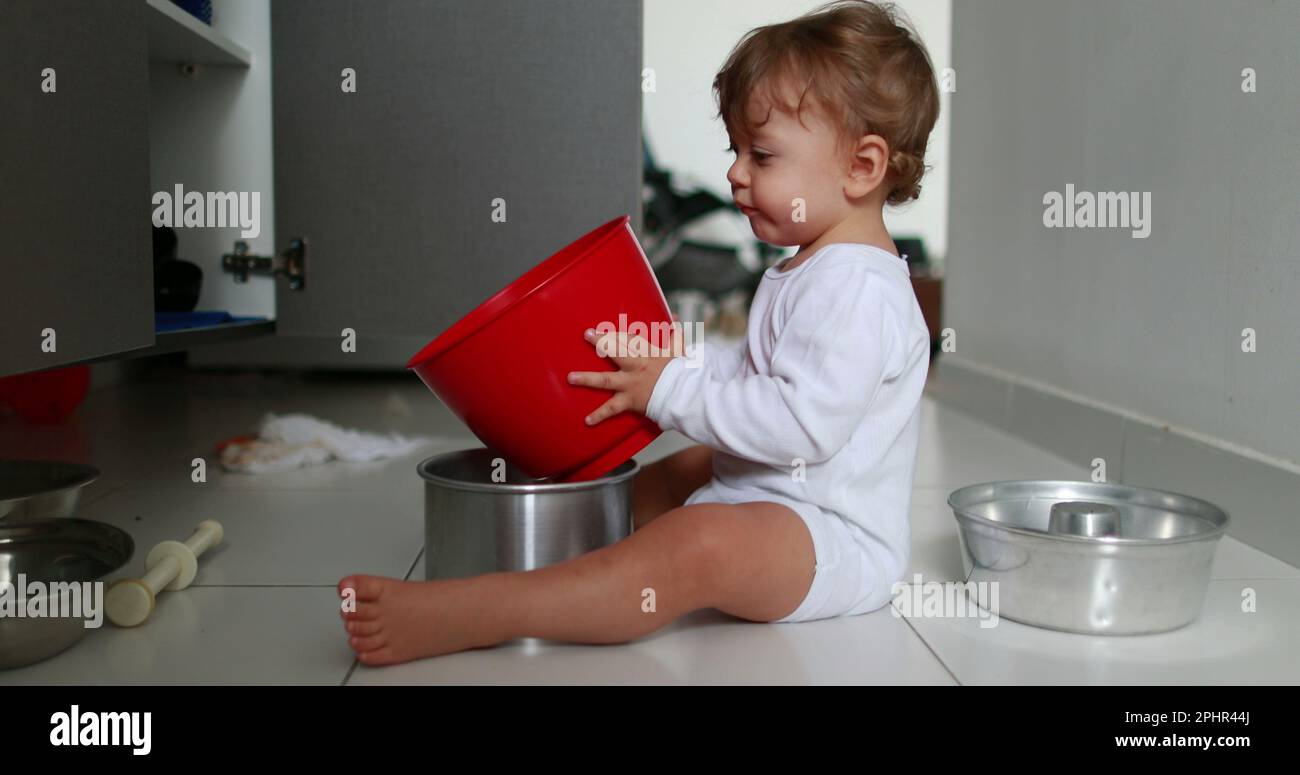 Cute baby on kitchen floor playing with kitchen utensils, playful one ...
