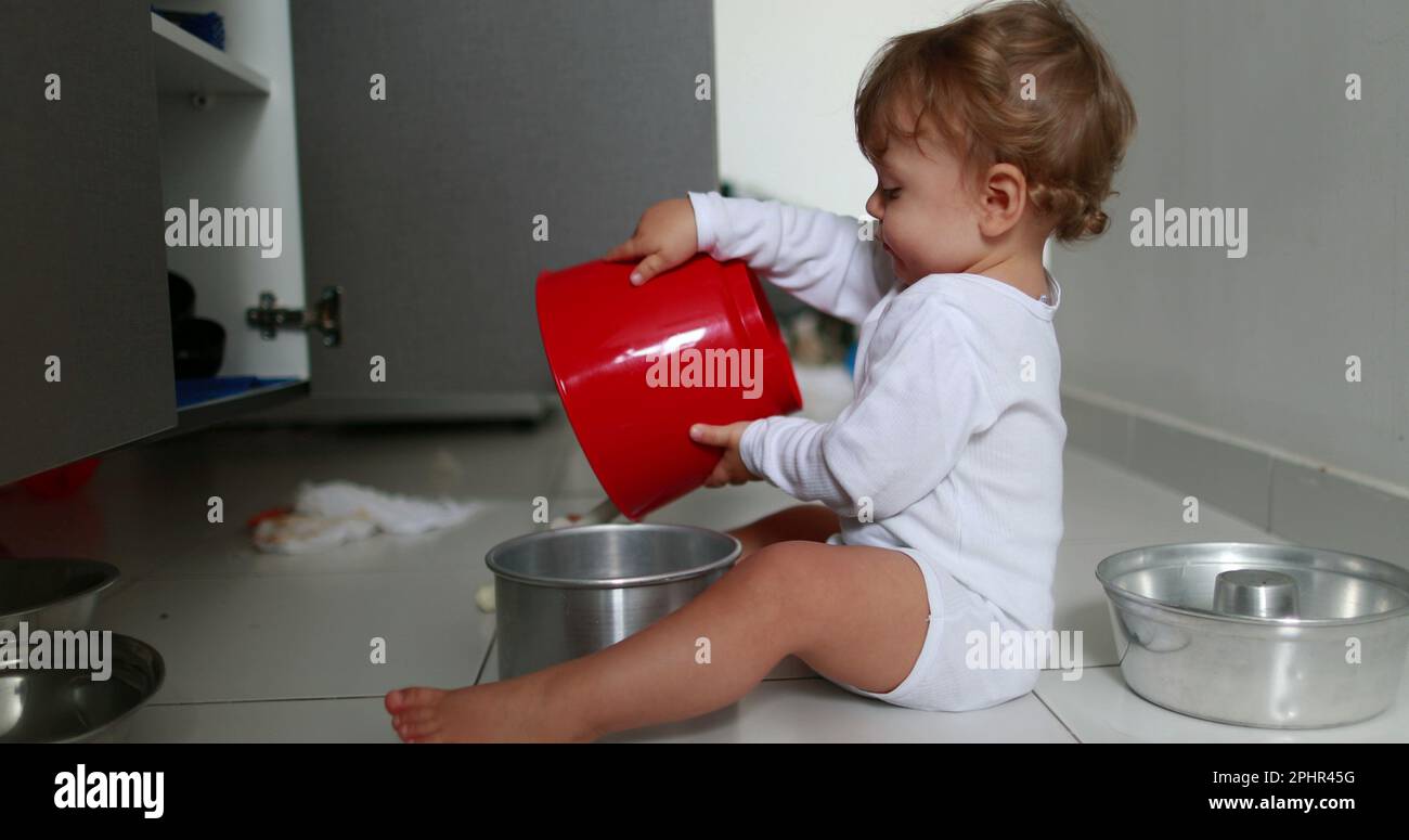 Cute baby on kitchen floor playing with kitchen utensils, playful one ...