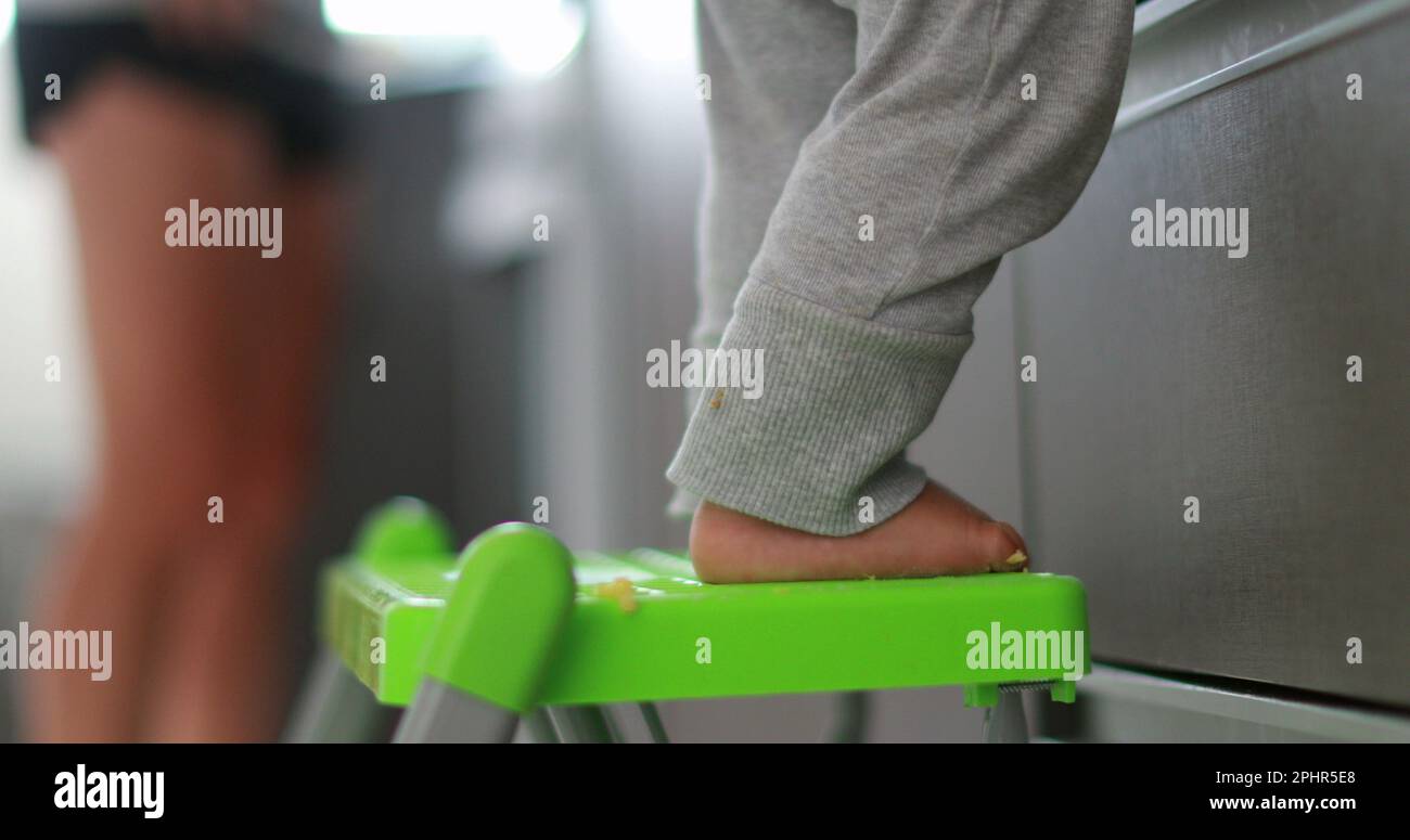 Child on tiptoes at kitchen helping mother. Infant one year old baby ...