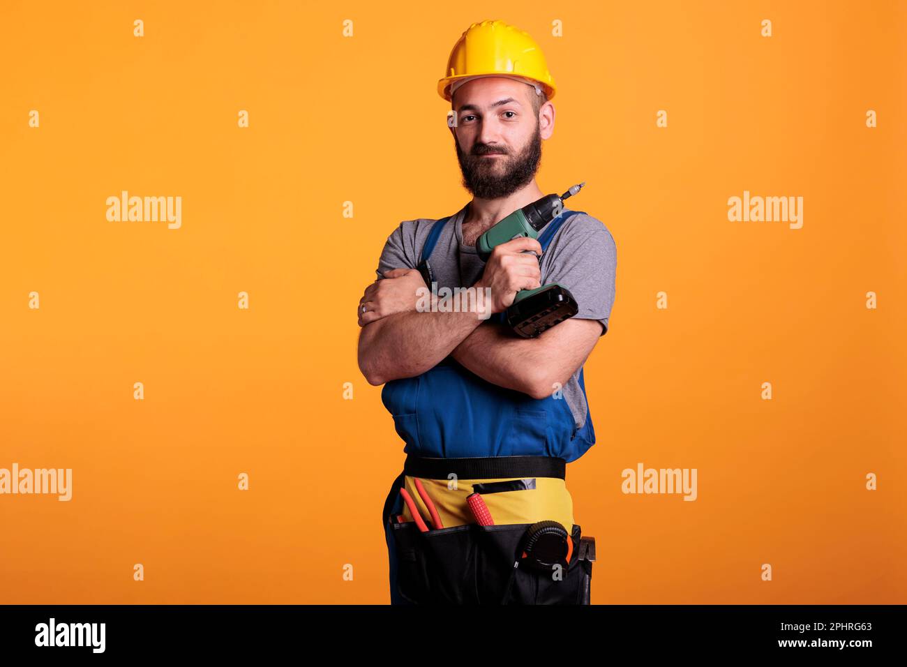 Professional builder holding cordless electric drill, posing in studio ...