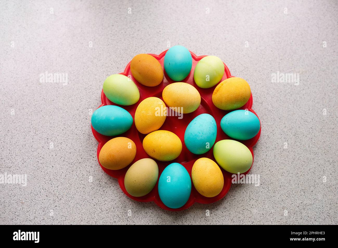 Bright Easter eggs lie on a red, round stand on a marble table ...