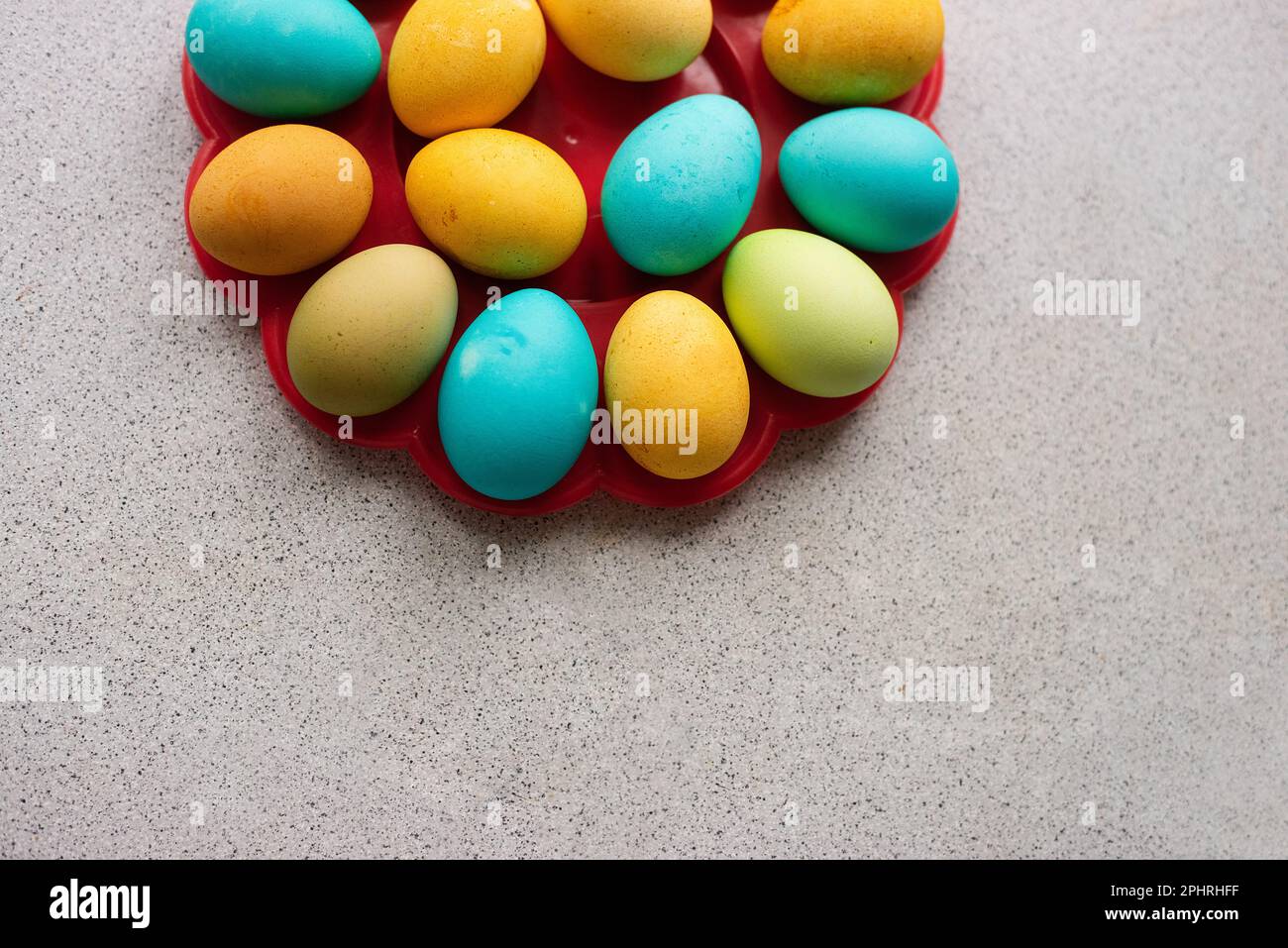 Bright Easter eggs lie on a red, round stand on a marble table ...