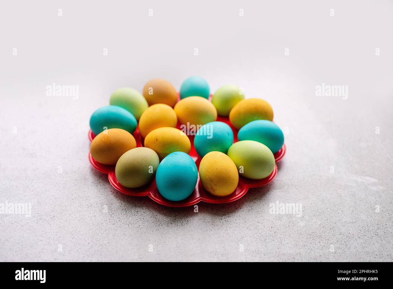 Bright Easter eggs lie on a red, round stand on a marble table ...