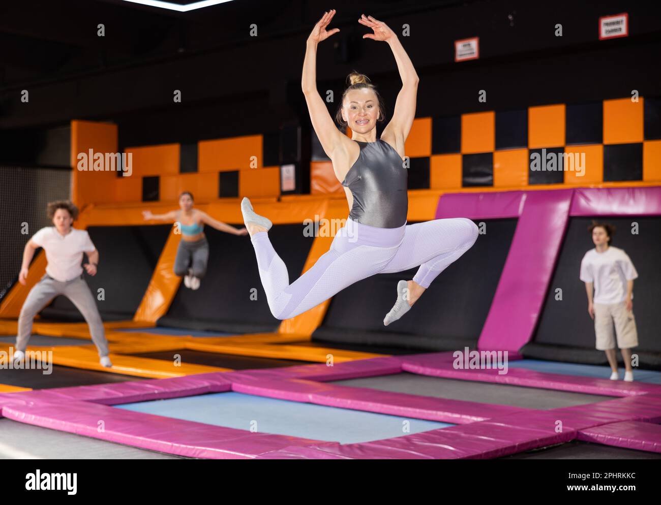 Middle-aged woman in sport clothes high jumping in trampoline arena ...