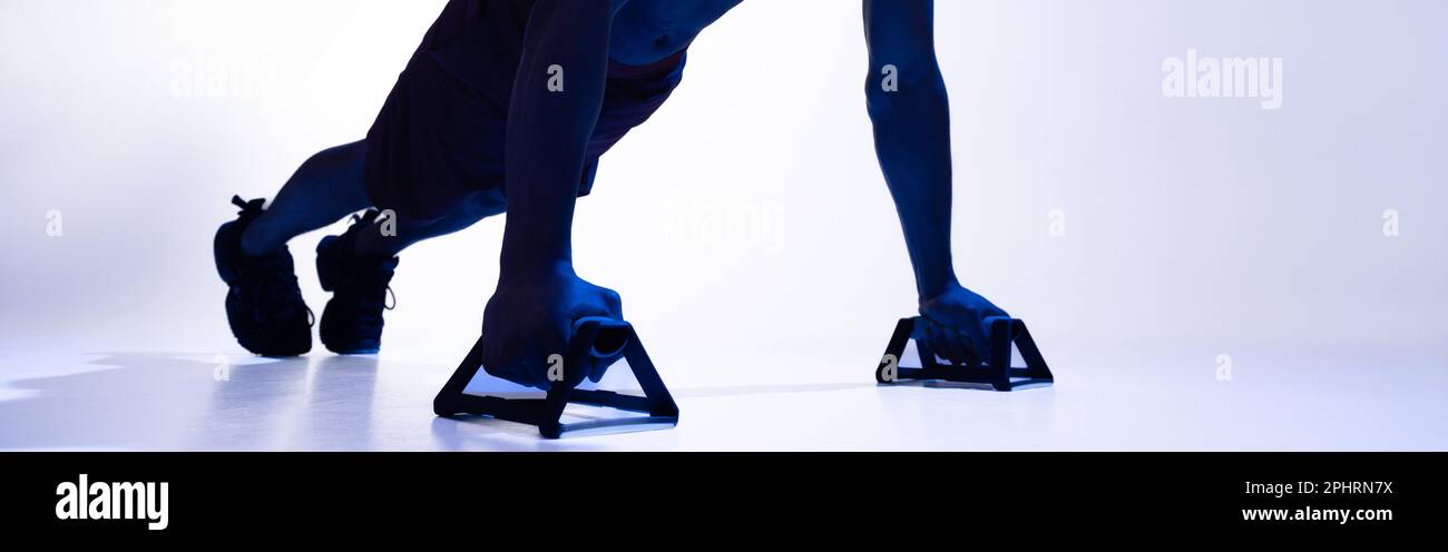 Athletic man is doing push ups while using special handles on studio ...