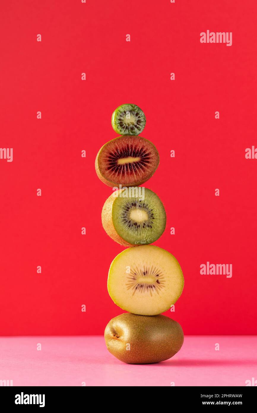 Still life with balancing kiwis of different varieties on a red. A ...