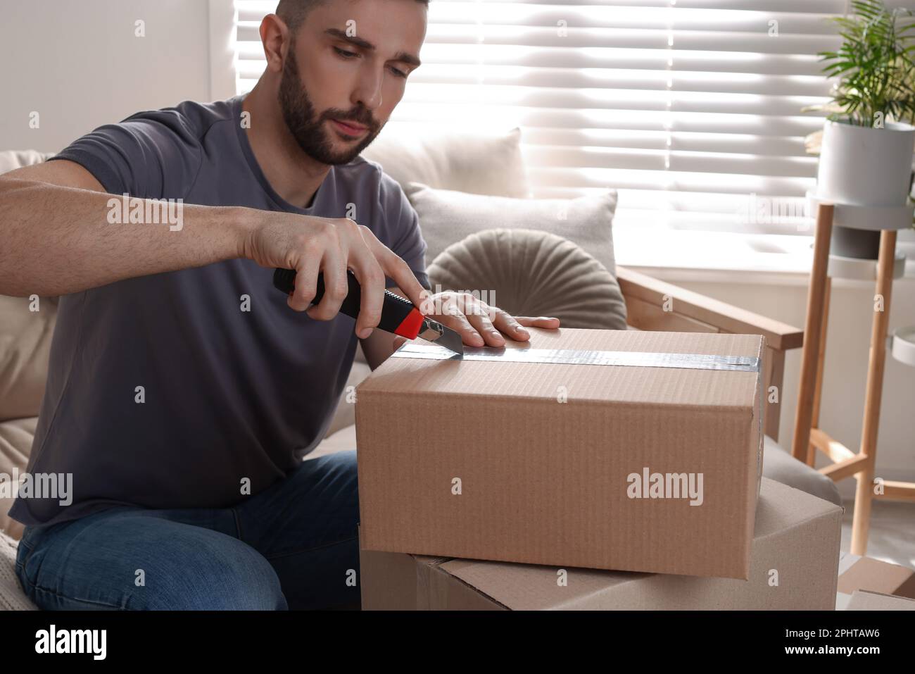 Man using utility knife to open parcel at home Stock Photo - Alamy