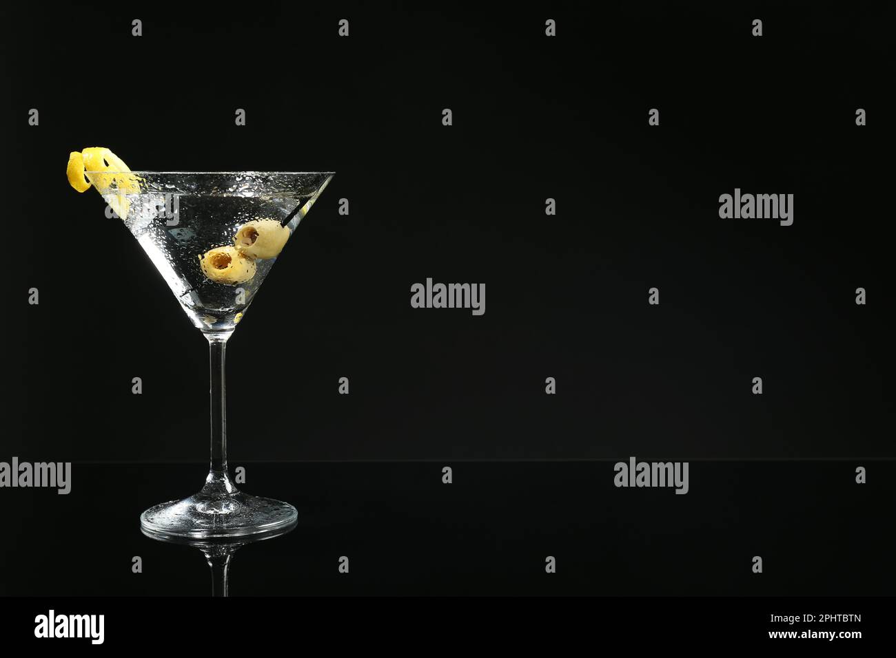Martini cocktail with olives and lemon twist on dark background, space ...