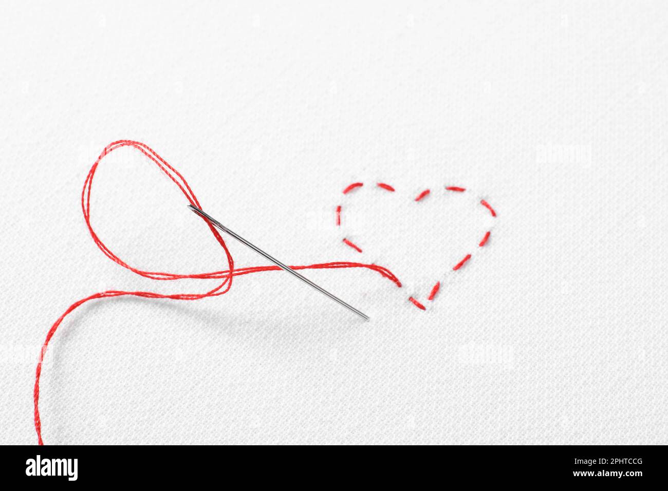 Needle with red thread and stitches in shape of heart on white fabric ...