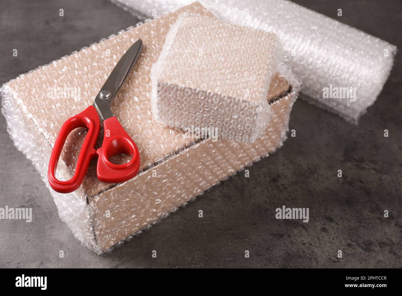 Cardboard boxes, bubble wrap and scissors on dark grey table Stock ...