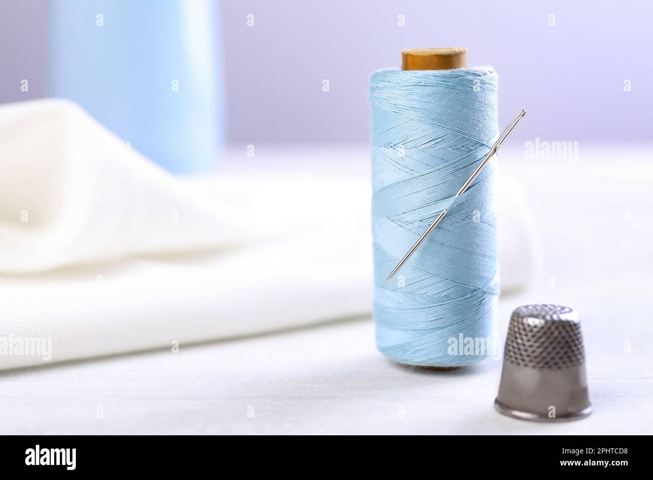 Spool of light blue sewing thread with needle and thimble on white ...