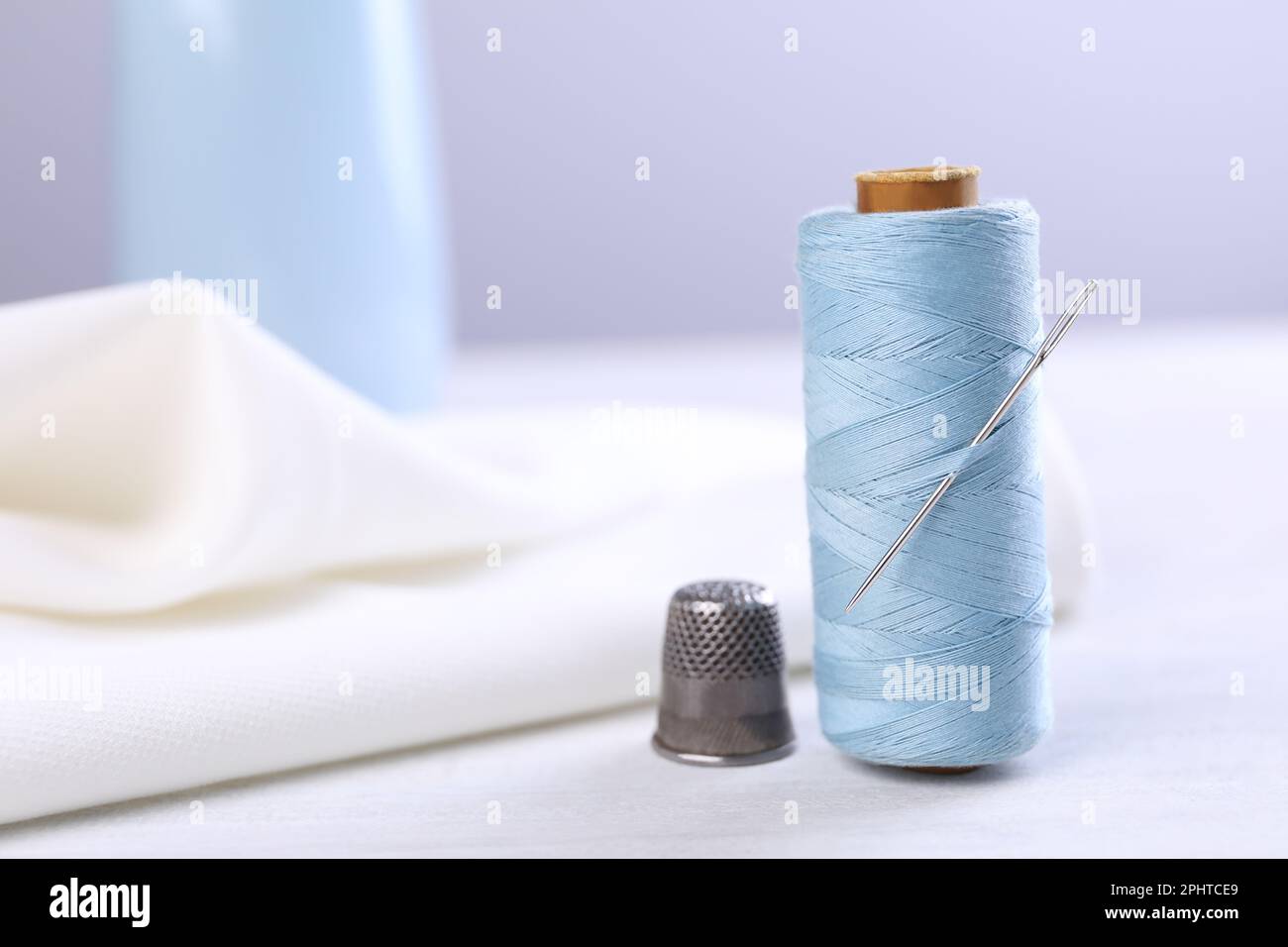 Spool of light blue sewing thread with needle and thimble on white ...