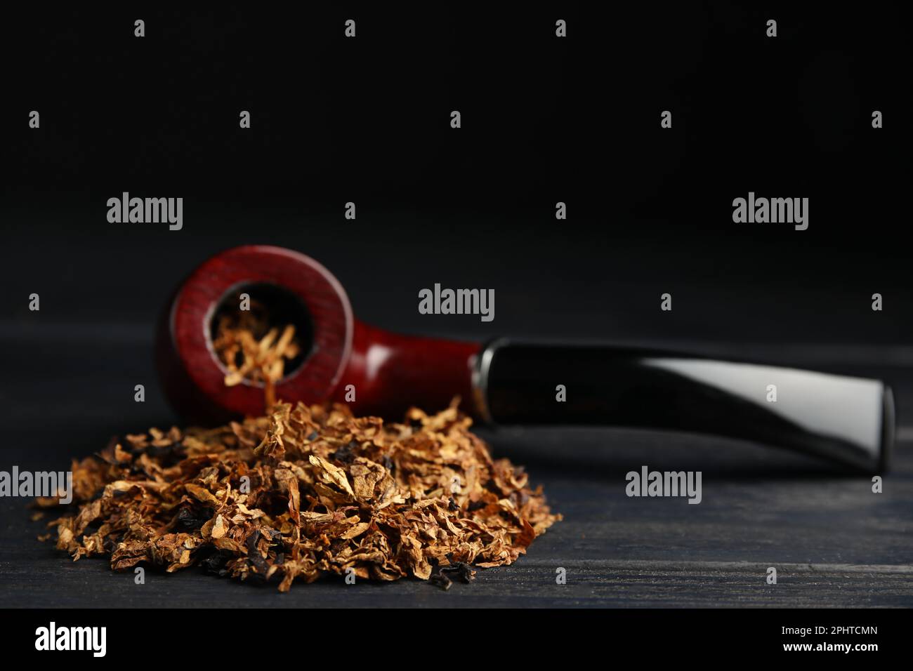 Smoking pipe and dry tobacco on black wooden table. Space for text ...