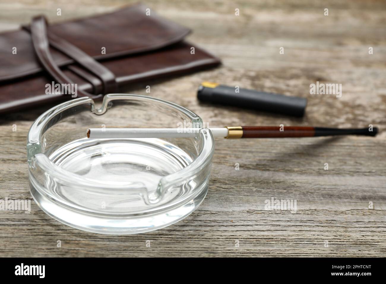Glass ashtray with long cigarettes holder, clutch and lighter on wooden ...