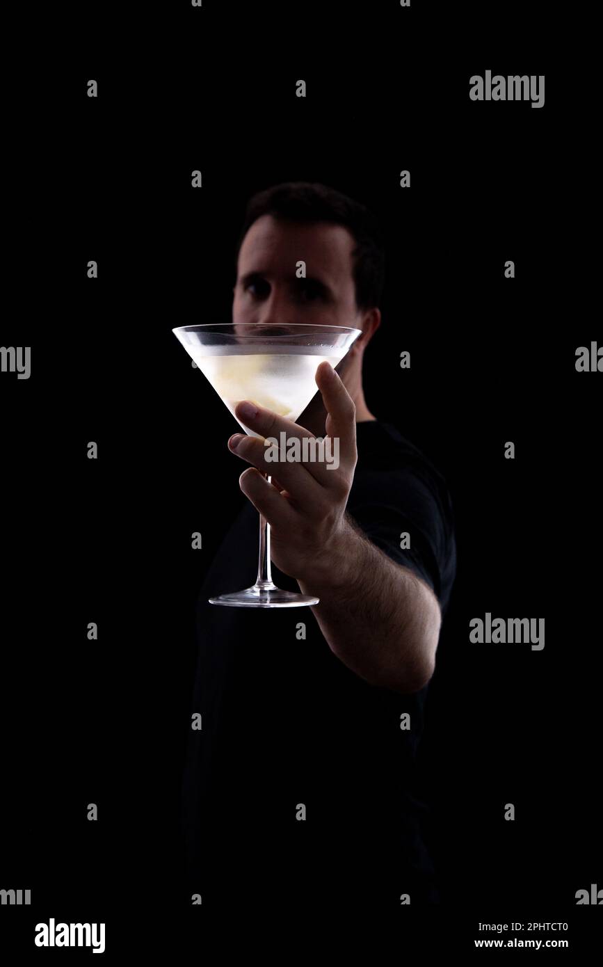 young man in a black shirt with a glass of martini isolated on a black ...