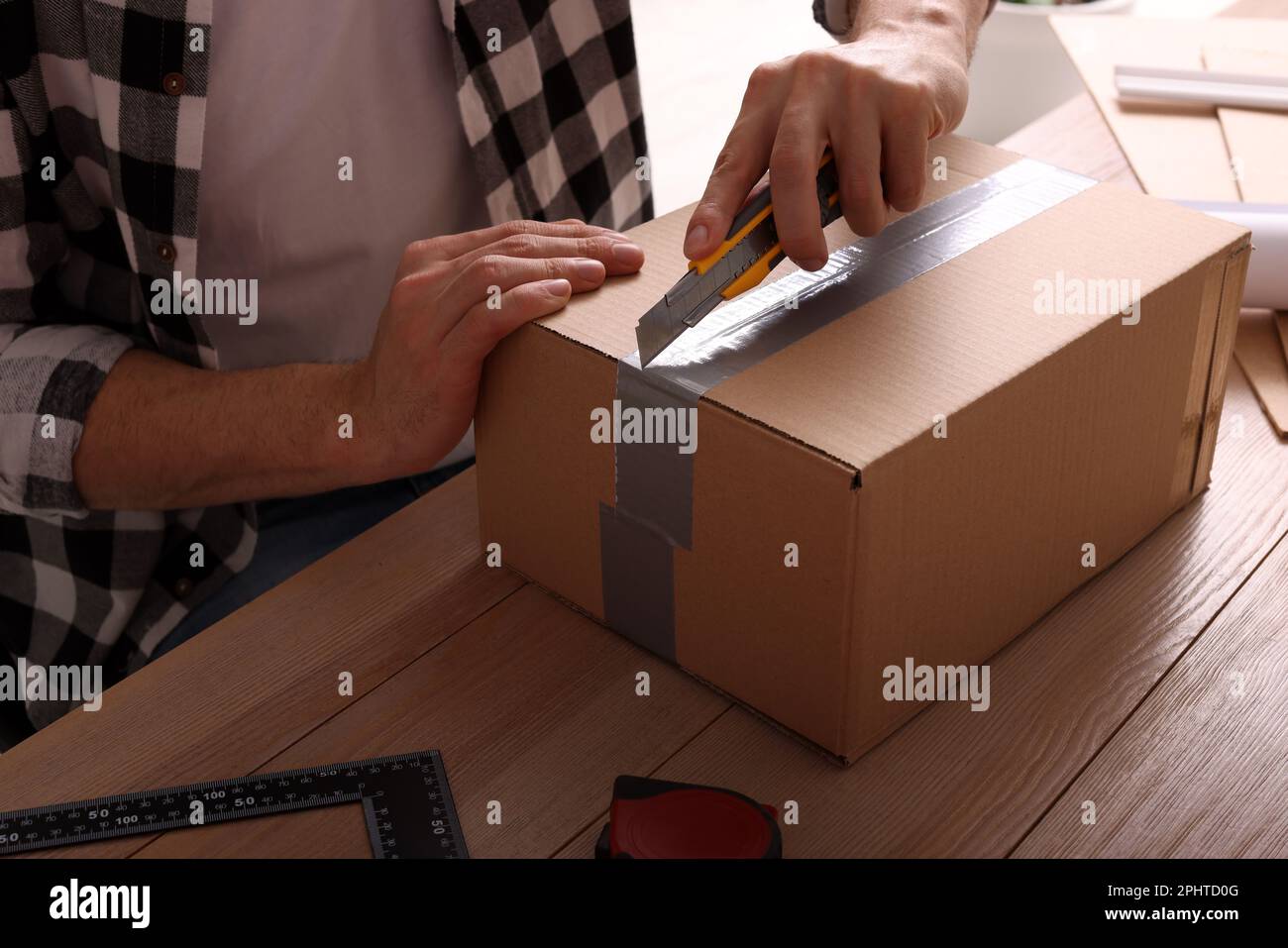 Man using utility knife to open parcel at wooden table, closeup Stock ...
