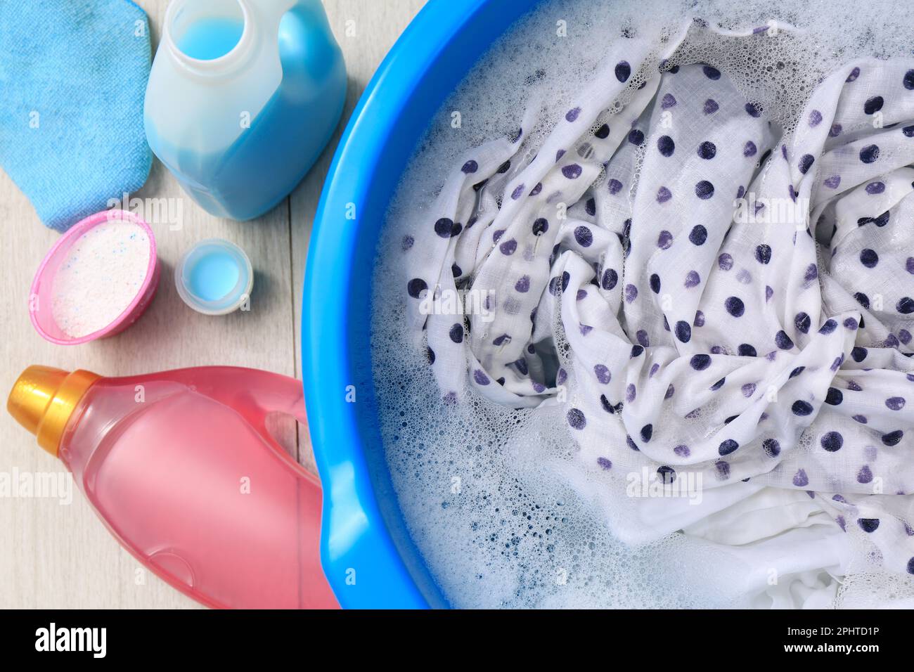 Basin with garment in suds near bottles of detergents and powder on ...