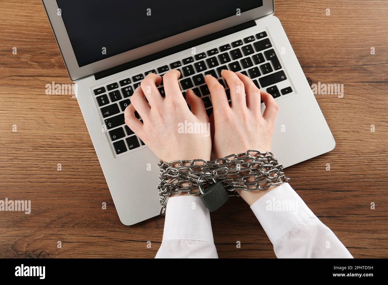 Woman with chained hands typing on laptop at wooden table, top view ...