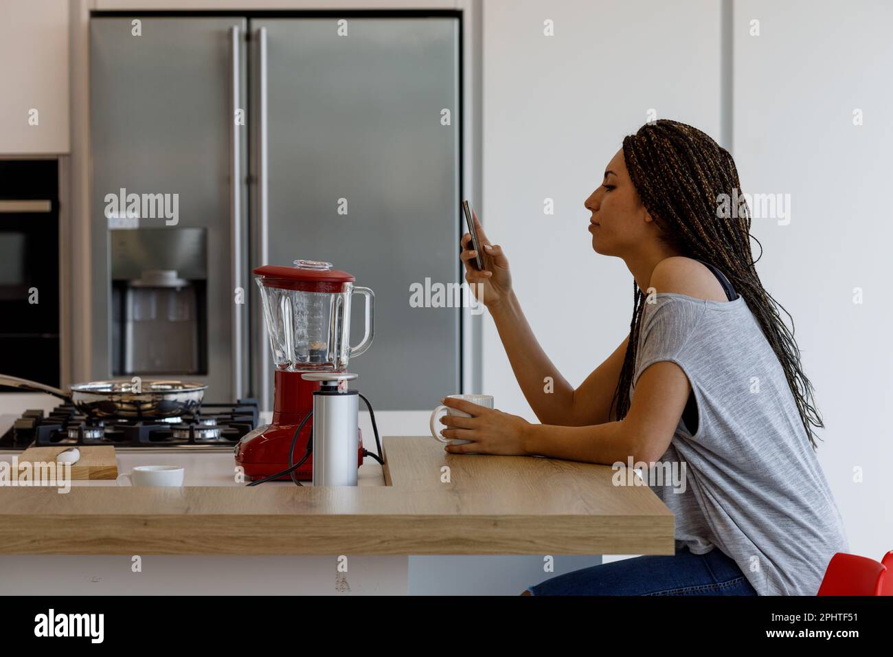 young woman uses her smartphone in the kitchen while having breakfast ...