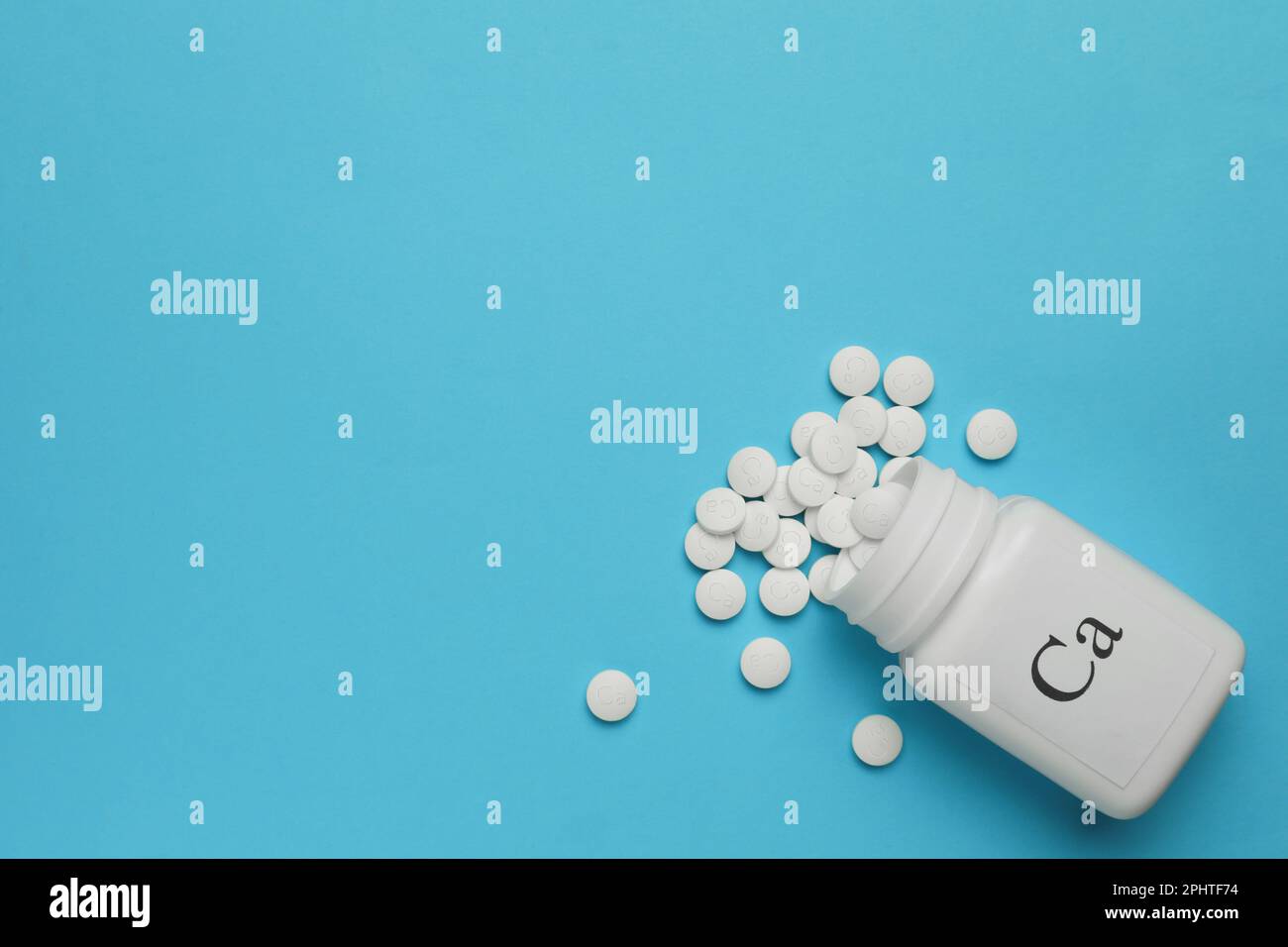 Overturned bottle of calcium supplement pills on light blue background ...