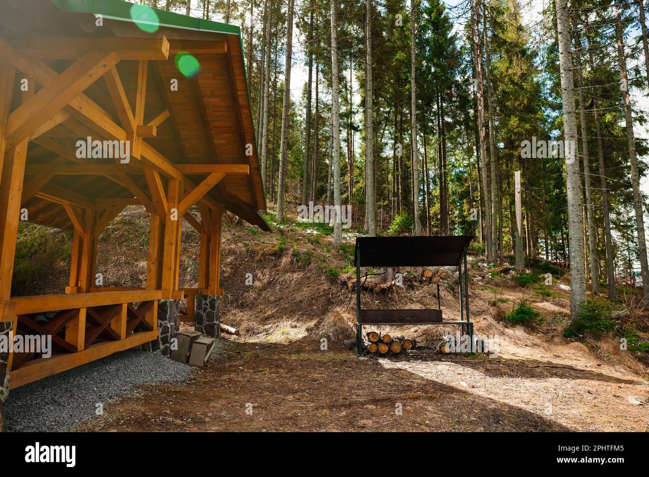 Metal barbecue with stacked firewood and wooden gazebo near forest on ...