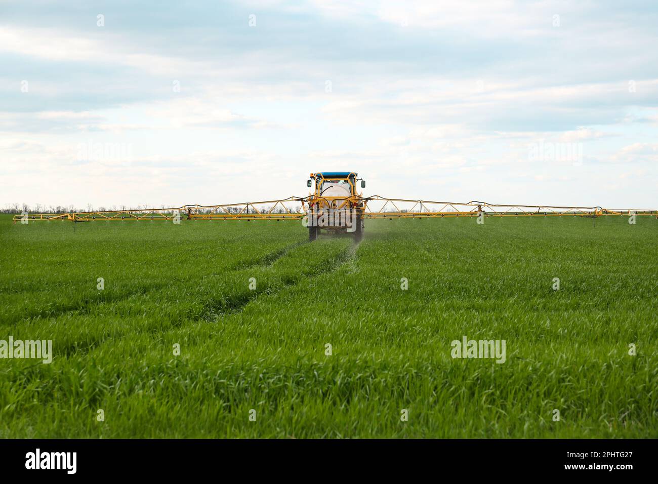 Tractor spraying pesticide in field on spring day. Agricultural ...