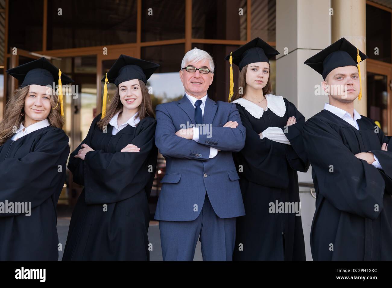 A professor and his students in graduation gowns stand with their arms ...