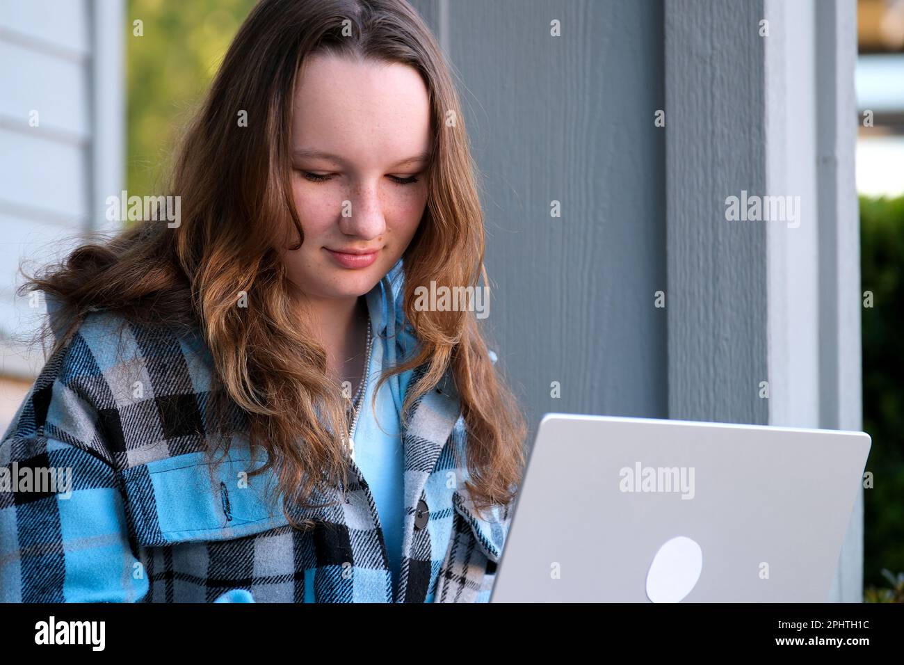 teenage girl with a laptop sitting on the porch of house. She watching ...