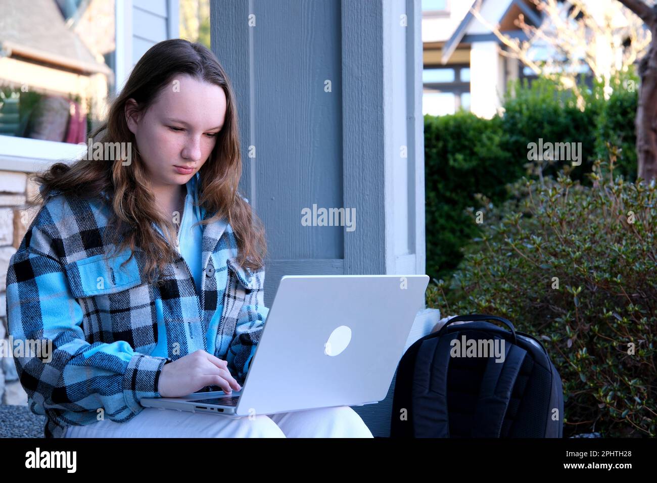 teenage girl with a laptop sitting on the porch of house. She watching ...