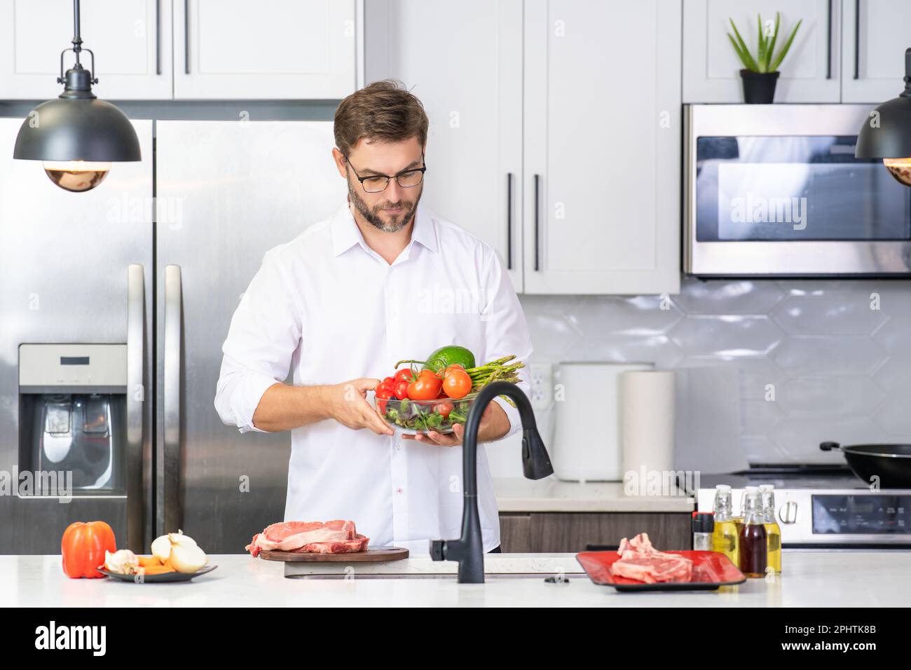 Handsome man cooking salad in kitchen. Guy cooking on kitchen with ...