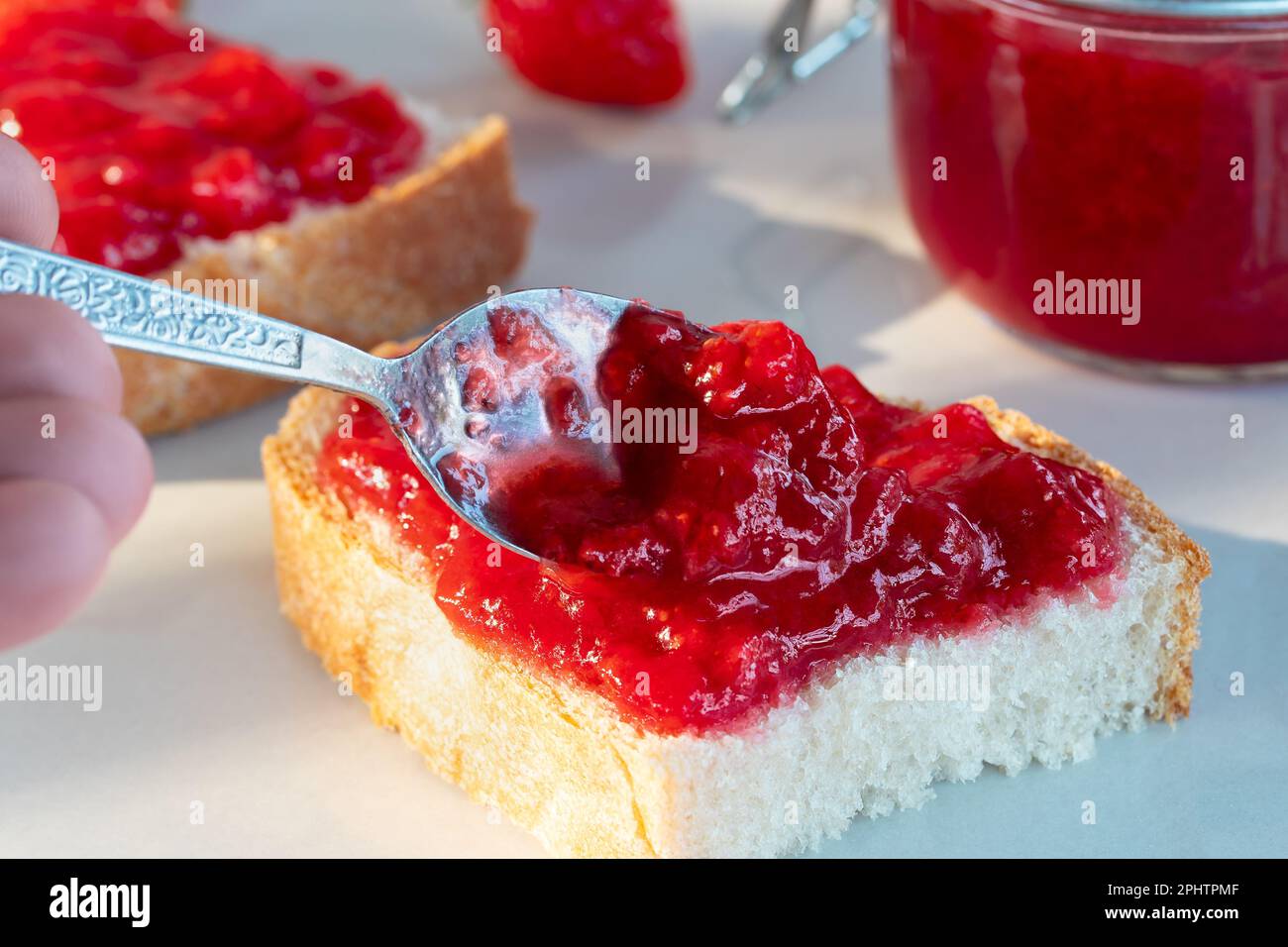 Spreading strawberry jam on a piece of wheat bread Stock Photo - Alamy