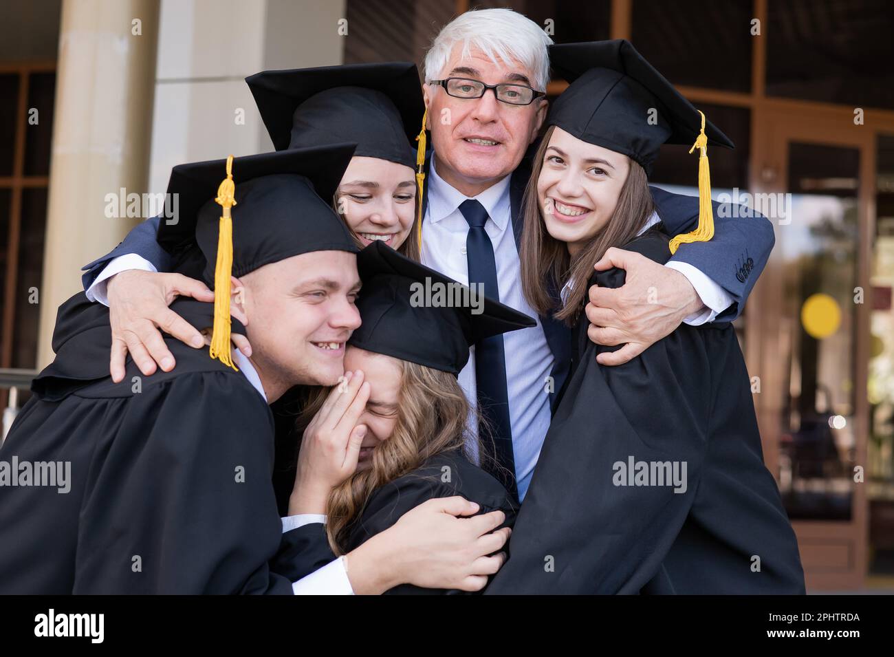 A gray-haired male teacher congratulates students on their graduation ...