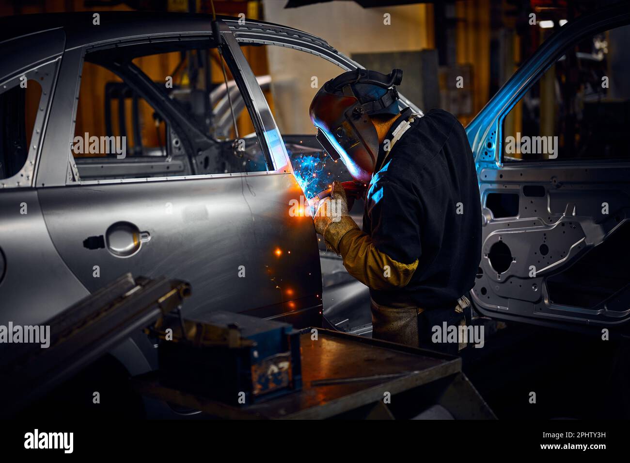 Welder in helmet works with metal parts of car carcass Stock Photo - Alamy
