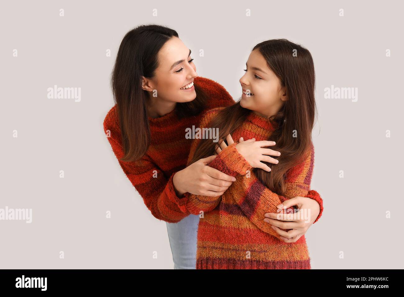 Little girl and her mother in warm sweaters hugging on grey background ...